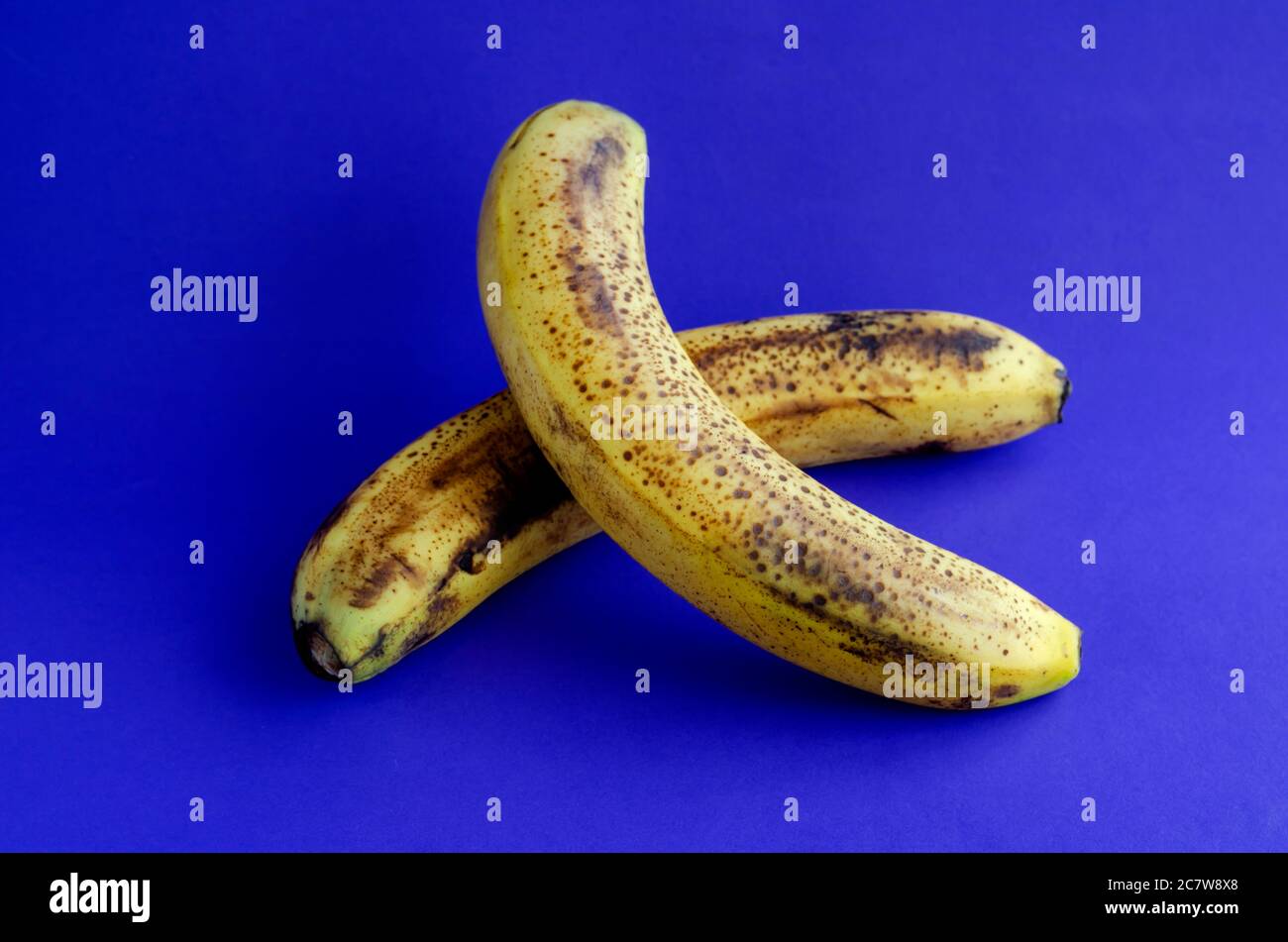 Two overripe bananas with brown spots on blue background. Ingredients ...