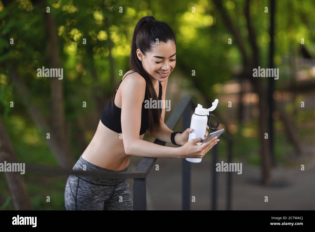 Sporty asian woman resting outdoors after running , using smartphone ...