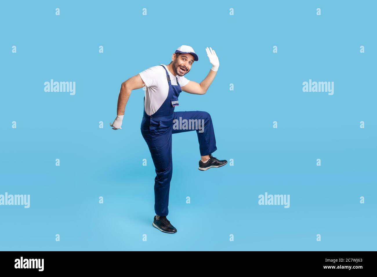 Full length funny happy handyman in blue uniform striding in big step ...