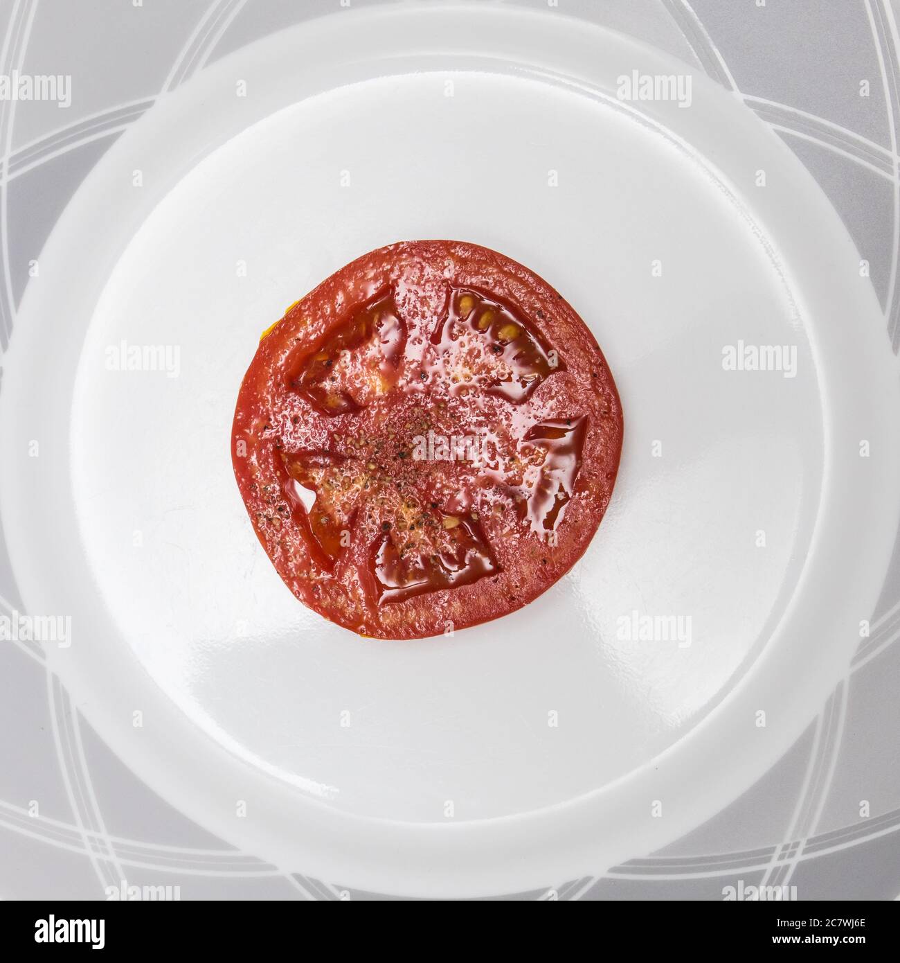 A single slice of a tomato from a home garden with salt and pepper ...