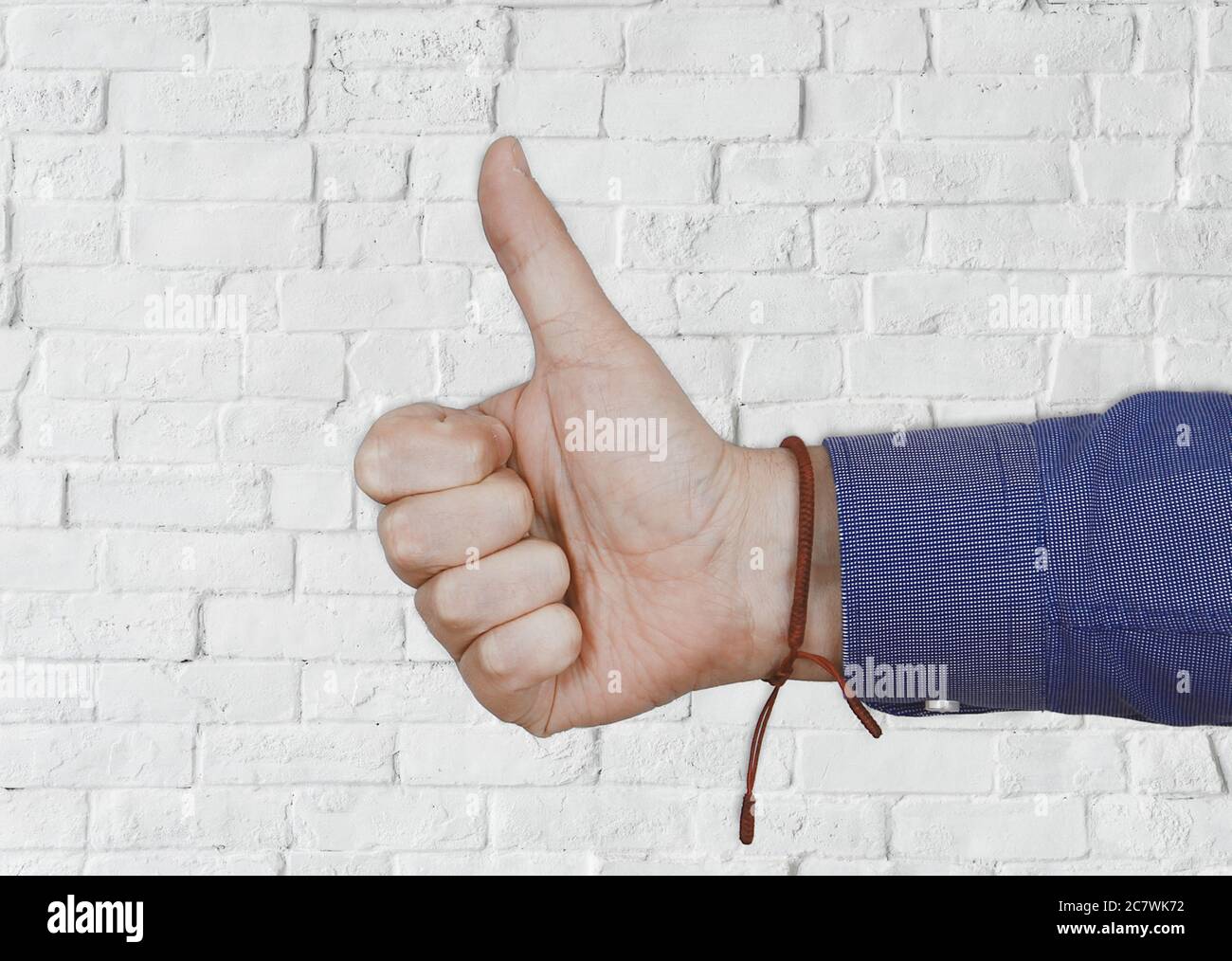 Closeup of a person doing the thumbs-up gesture with a white wall on ...