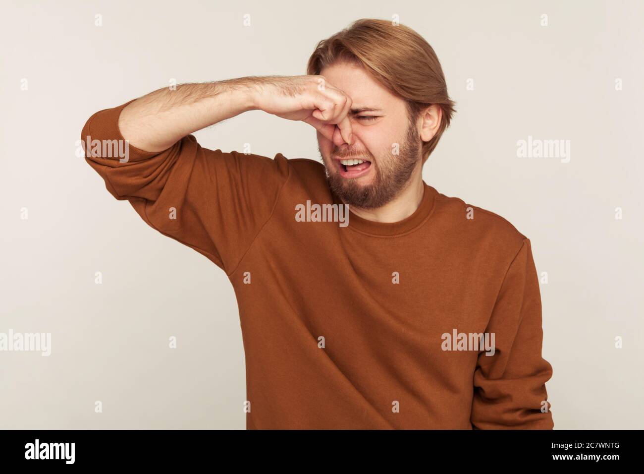 Bad smell. Portrait of bearded man grabbing nose, holding breath and grimacing in disgust ...
