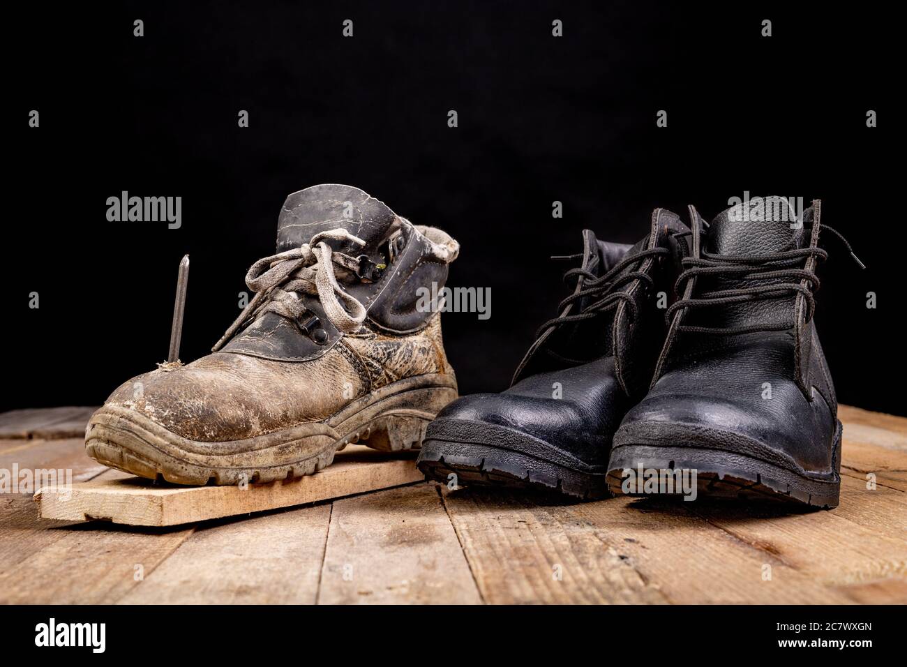 Old work shoe pierced with a nail. New work shoes. Dark background ...