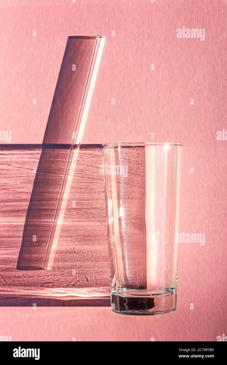 Empty drinking glass and glass straw form the shadow on pink background ...