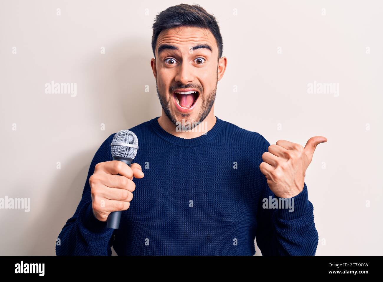 Young handsome singer man with beard singing song using microphone over white background ...