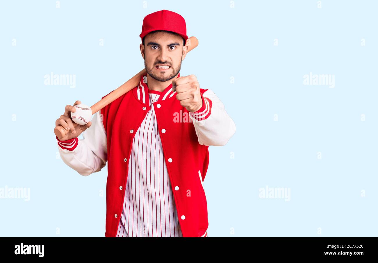Young handsome man holding baseball bat and ball annoyed and frustrated ...