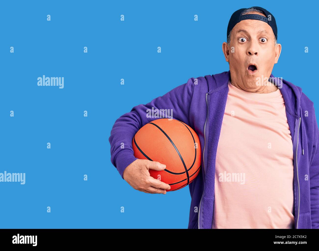 Senior handsome grey-haired man holding basketball ball scared and ...