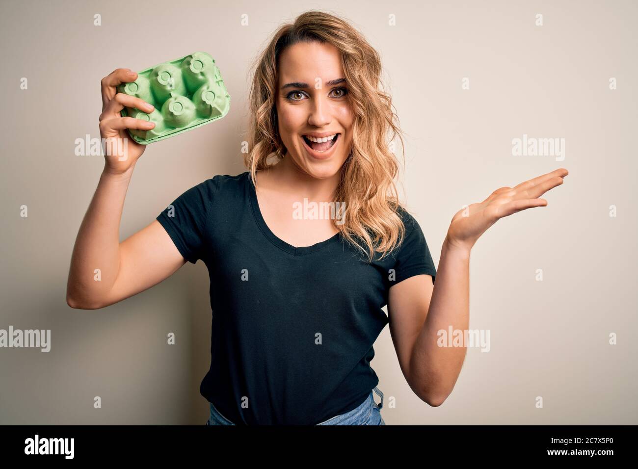 Young beautiful blonde woman holding box with fresh eggs over isolated ...