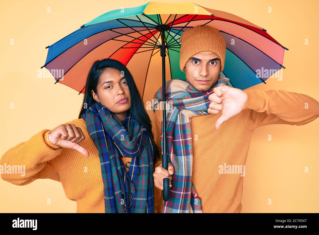 Beautiful latin young couple under colorful umbrella with angry face ...