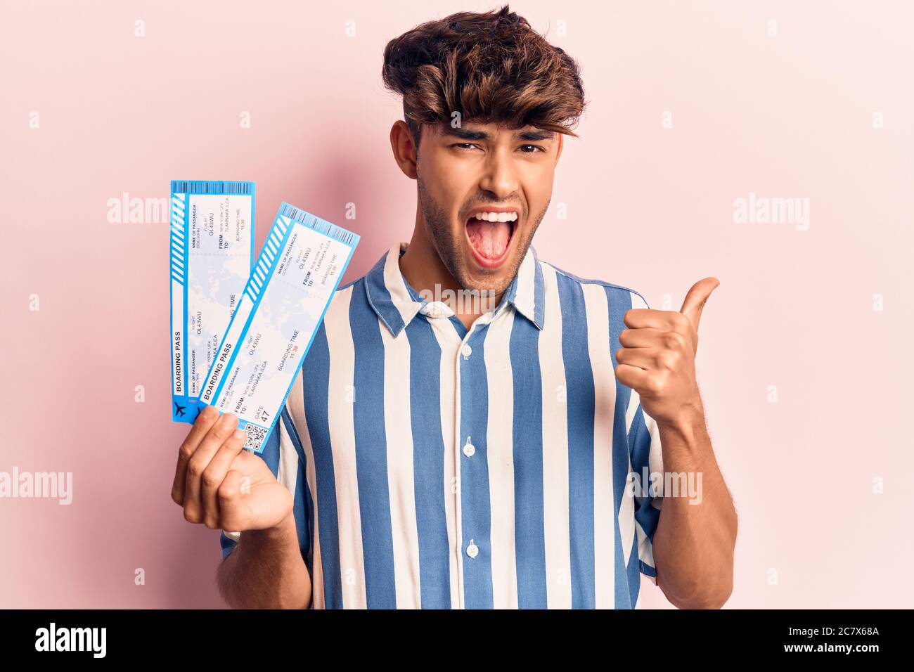 Young hispanic man holding boarding pass pointing thumb up to the side ...