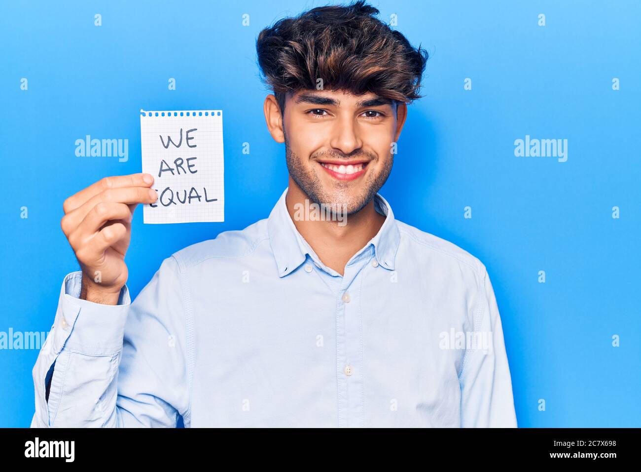 Young hispanic man holding we are equal paper looking positive and ...