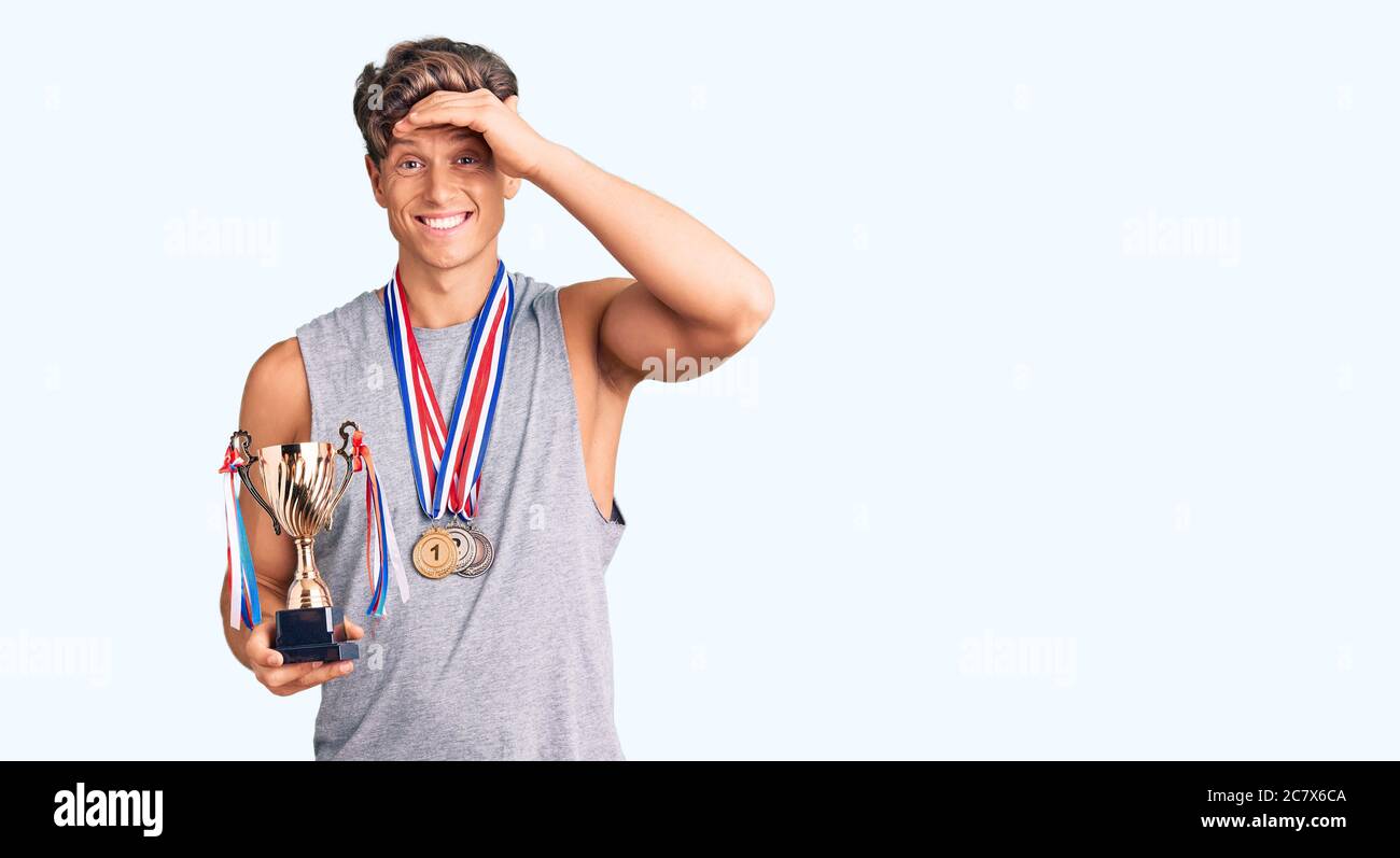 Young handsome man holding champion trophy wearing medals stressed and ...