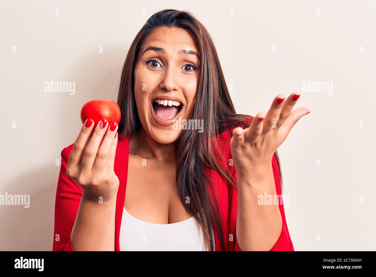 Young beautiful brunette woman holding tomato celebrating achievement ...