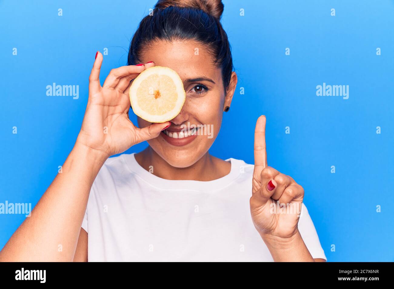 Young beautiful brunette woman holding slice of lemon smiling with an ...