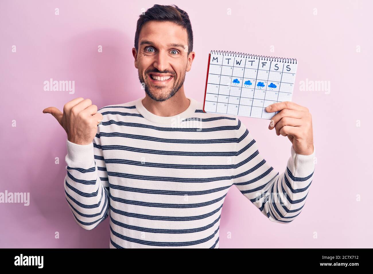Young handsome man holding weather calendar showing rainy week over ...