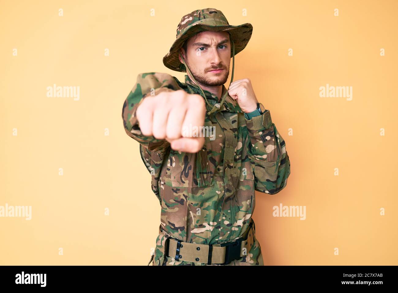 Young caucasian man wearing camouflage army uniform punching fist to ...