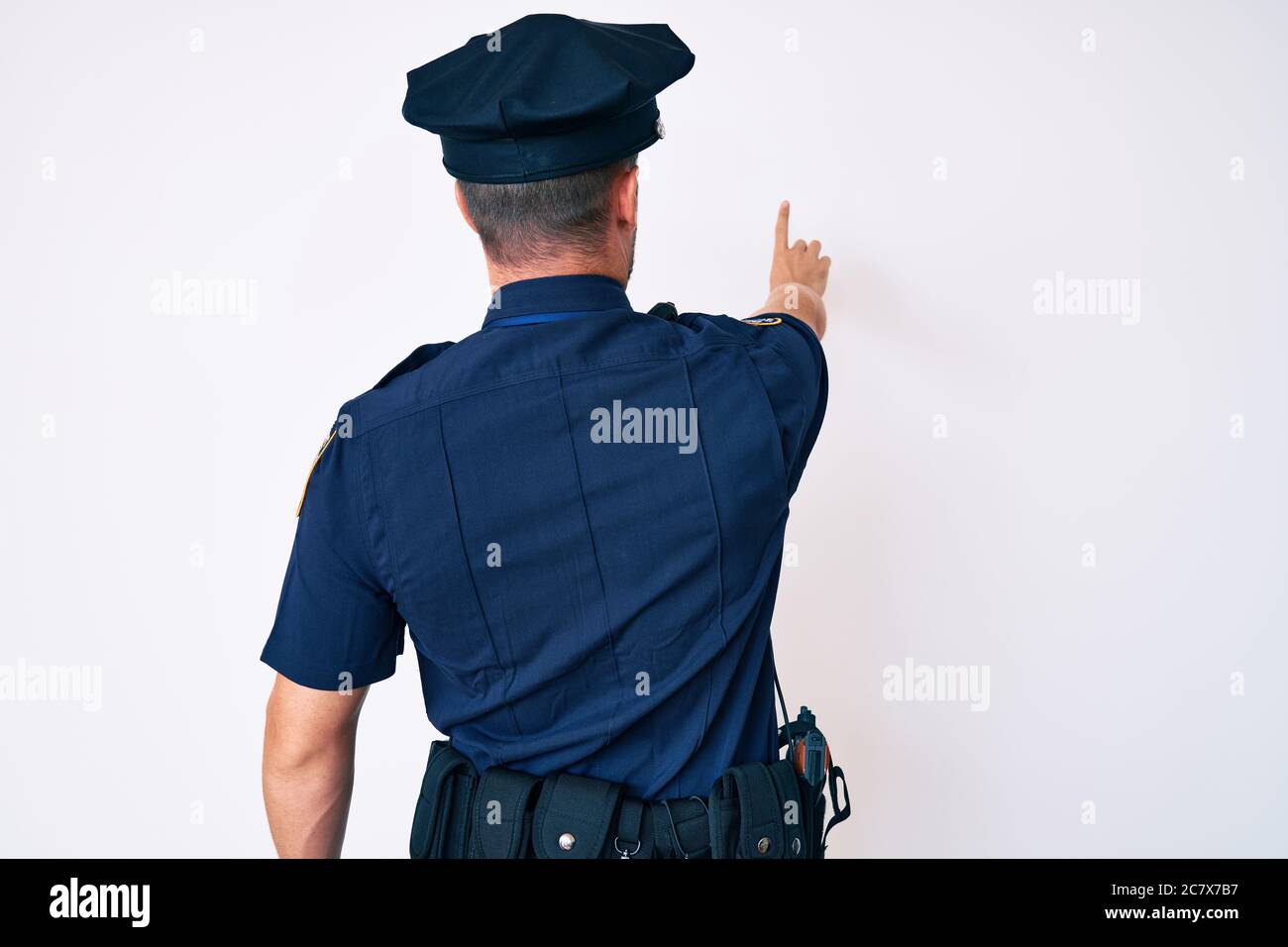 Young caucasian man wearing police uniform posing backwards pointing ...