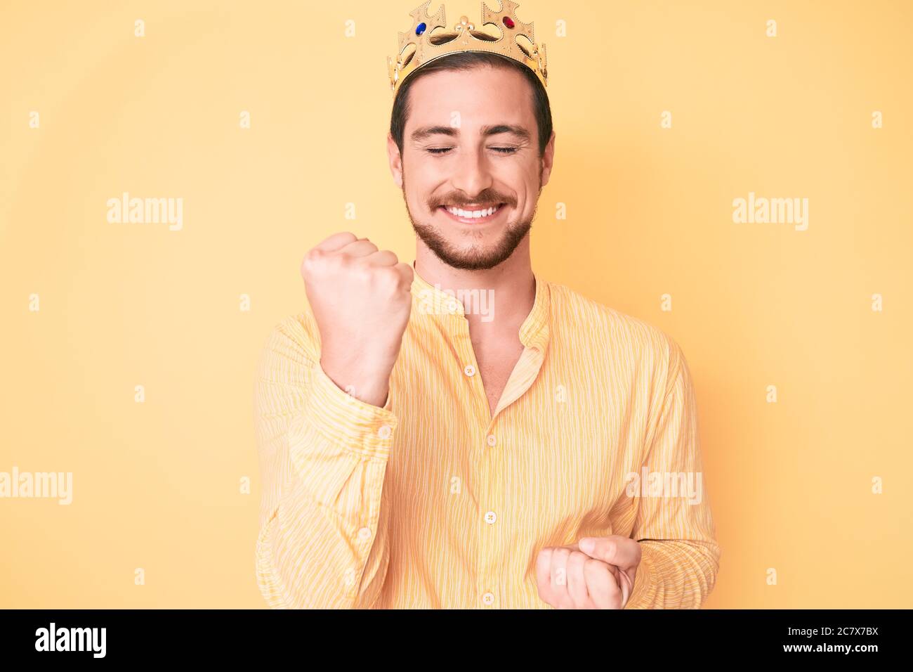 Young handsome man wearing king crown celebrating surprised and amazed ...