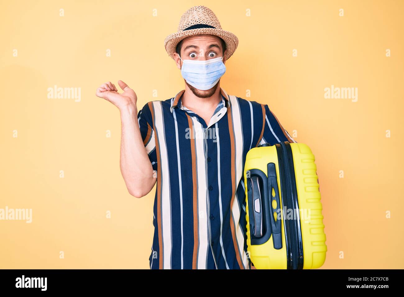 Young handsome man wearing medical mask holding suitcase screaming ...
