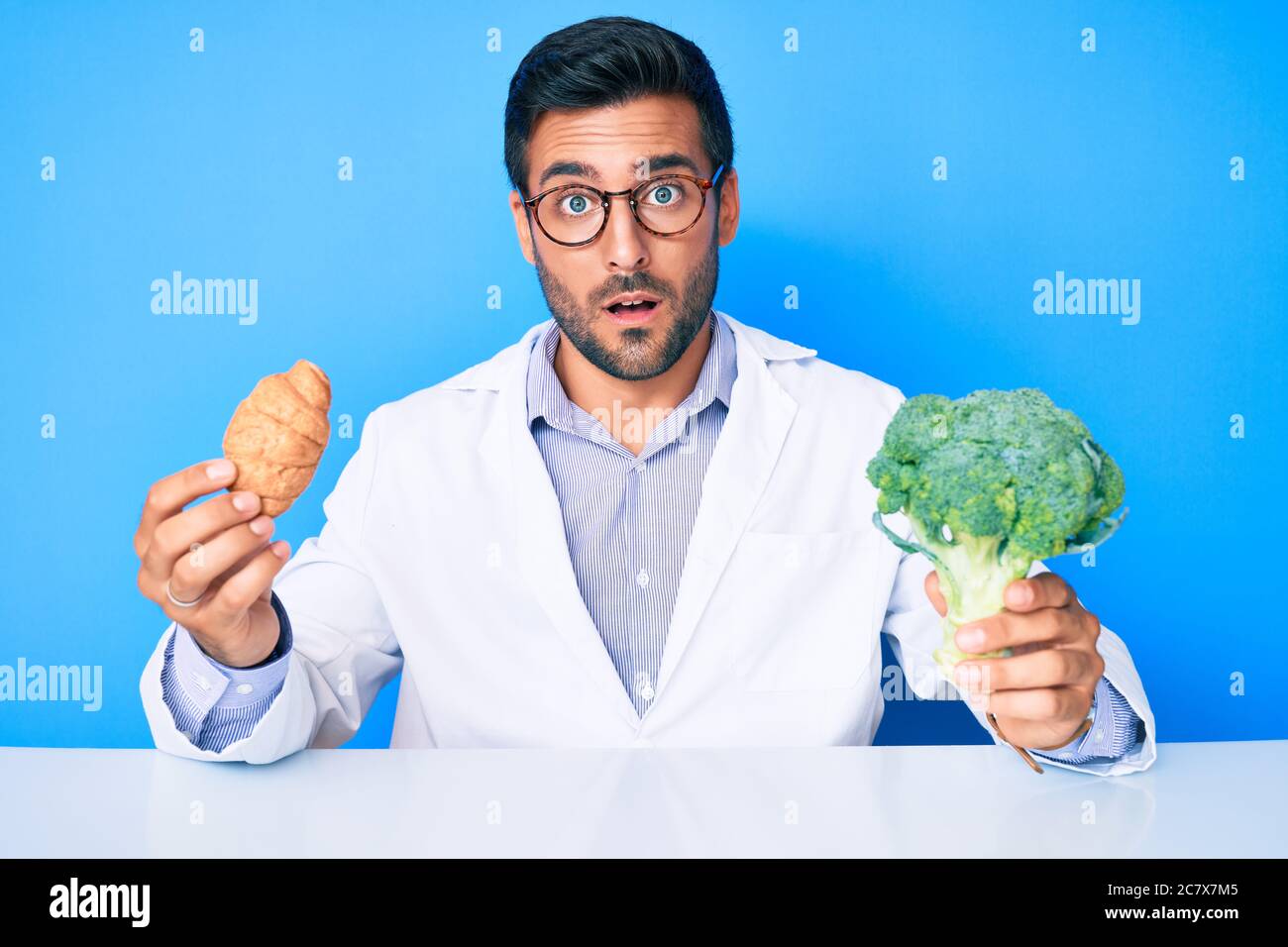 Young hispanic man as nutritionist doctor holding croissant and ...