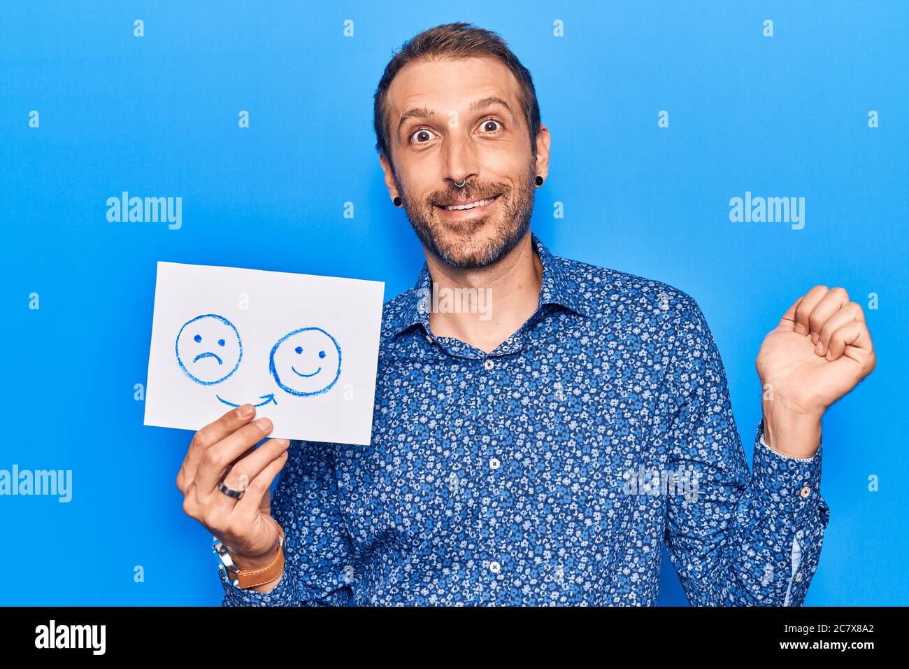 Young handsome man holding sad to happy emotion paper screaming proud ...