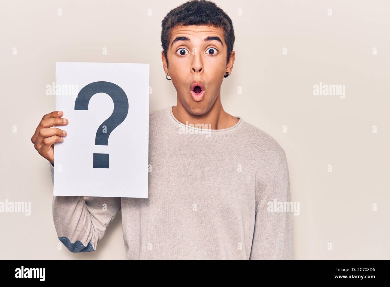 Young african amercian man holding question mark scared and amazed with ...