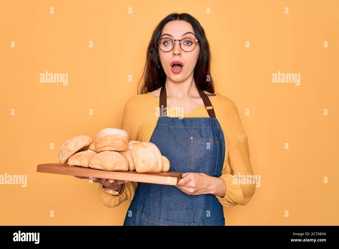 Young beautiful baker woman with blue eyes wearing apron holding tray ...