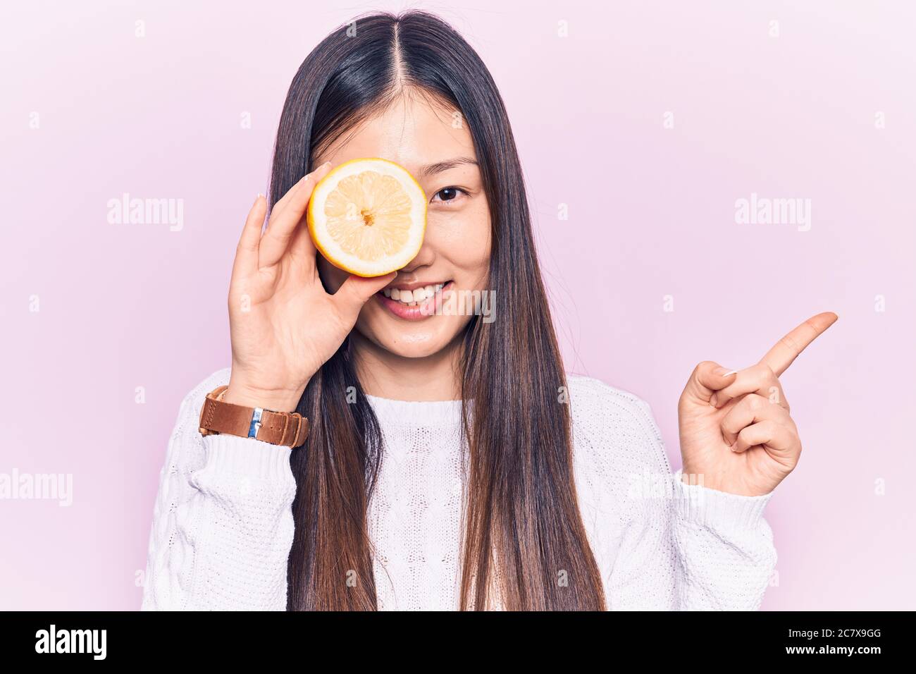 Young beautiful chinese woman holding slice of lemon over eye smiling ...