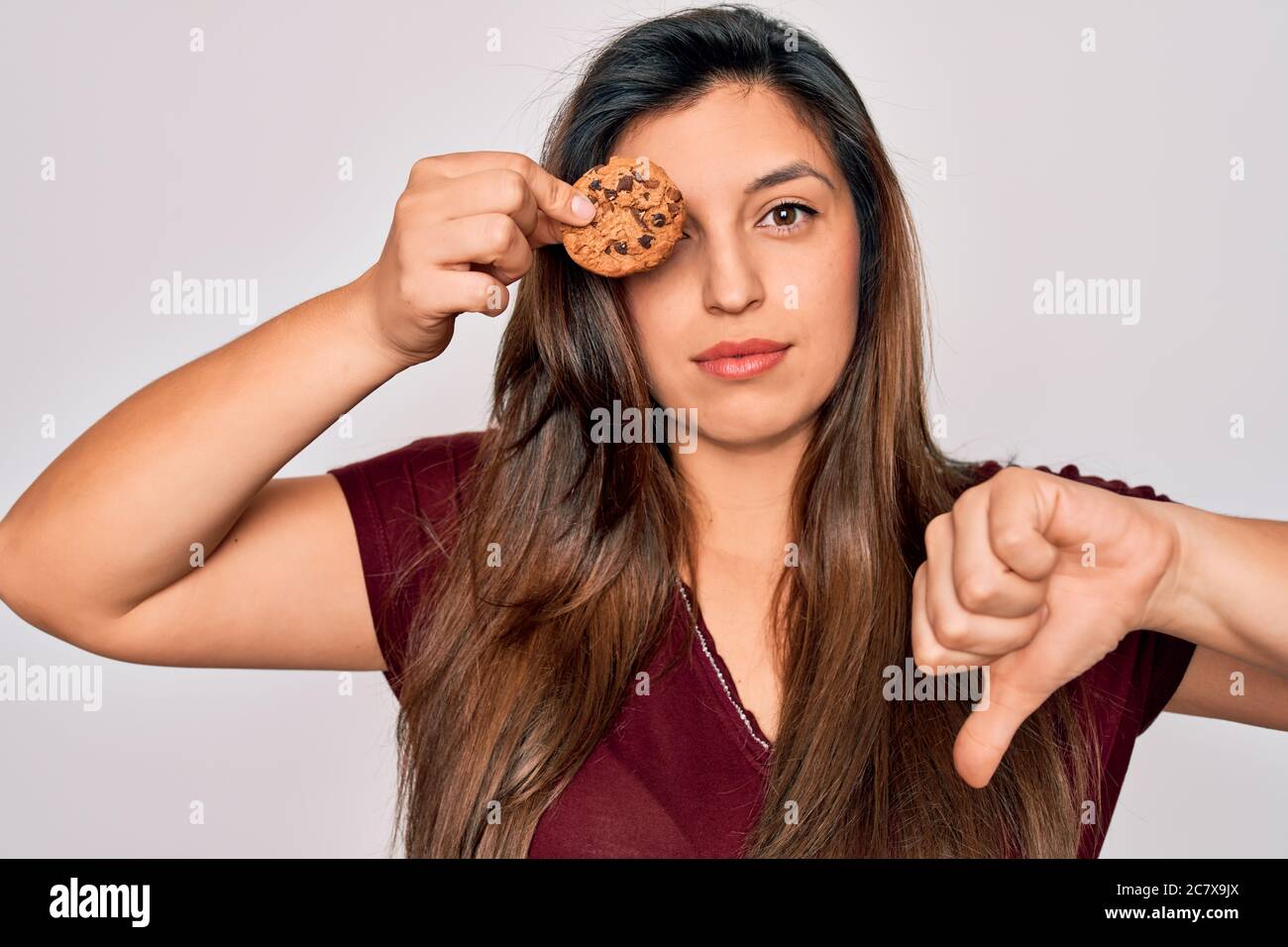 Young hispanic woman eating sweet chocolated chips cookie over isolated ...