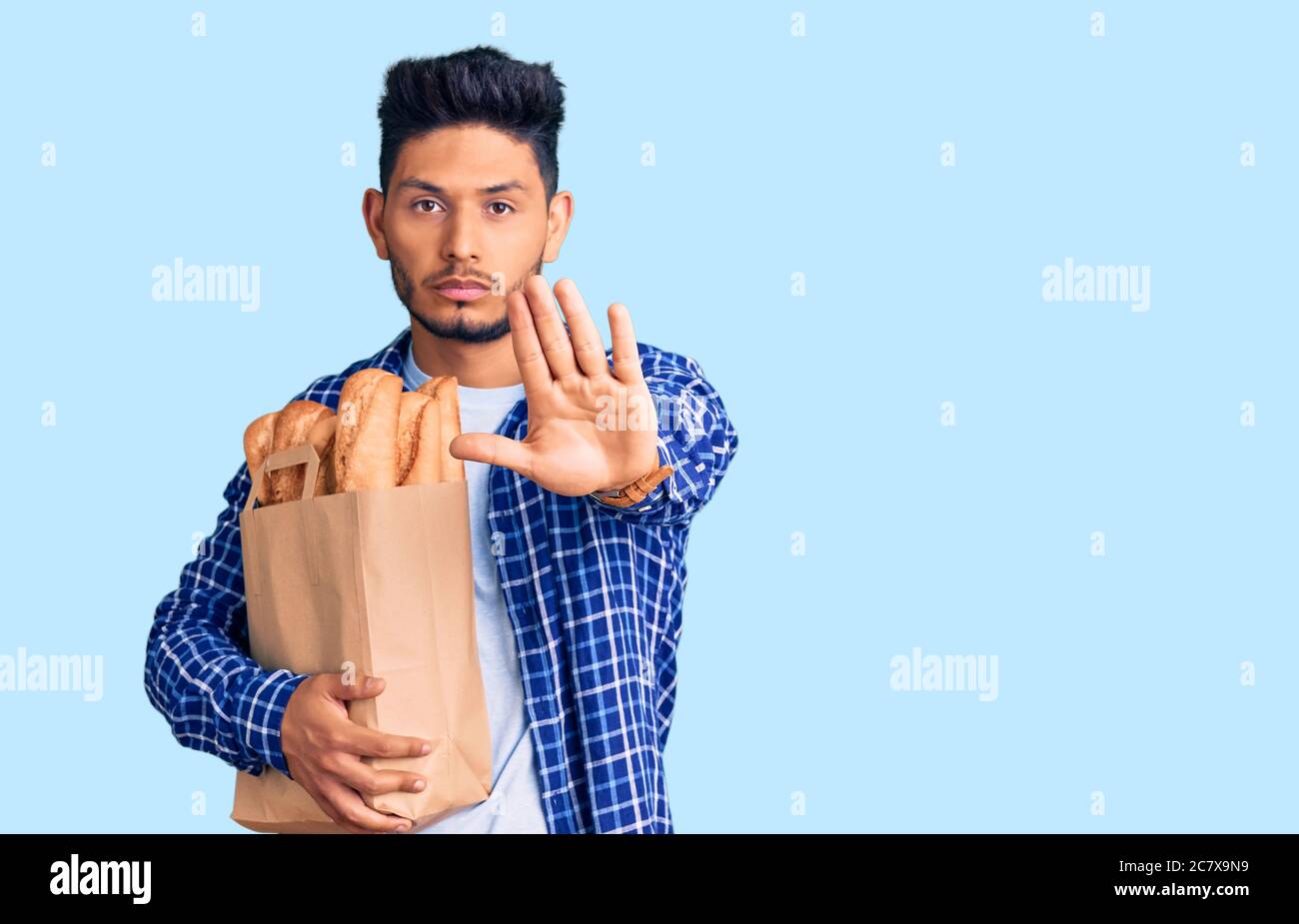 Handsome latin american young man holding paper bag with bread doing ...