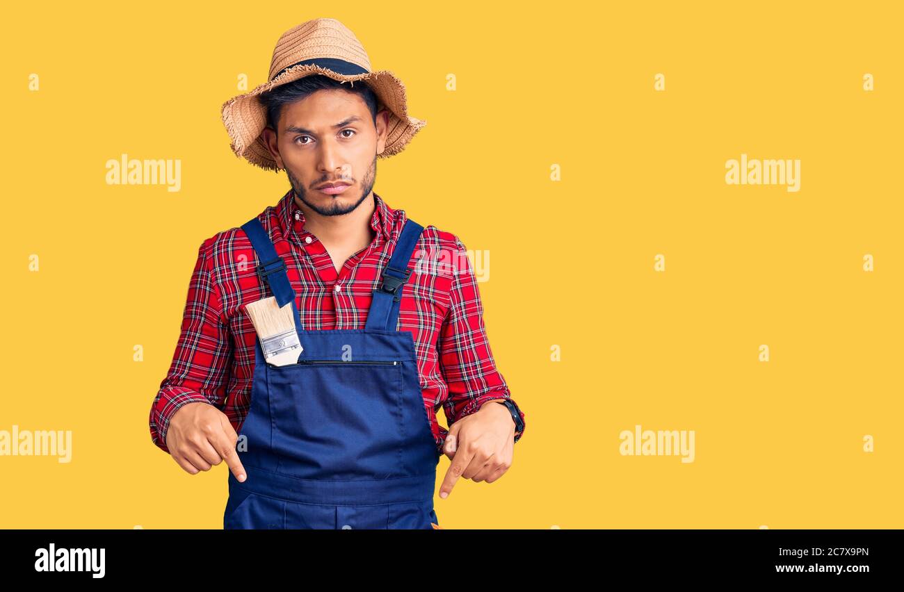 Handsome latin american young man weaing handyman uniform pointing down ...
