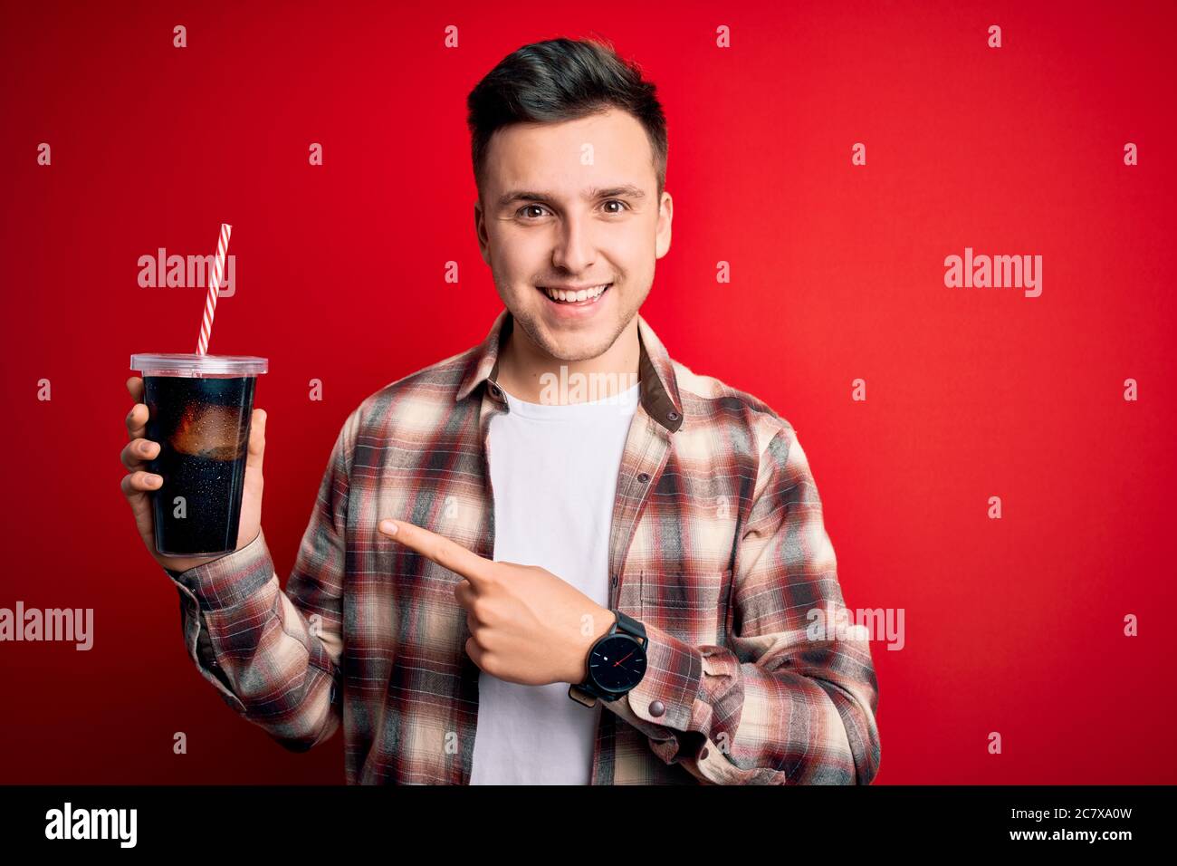 Young handsome caucasian man drinking a fresh soda refreshment over red ...