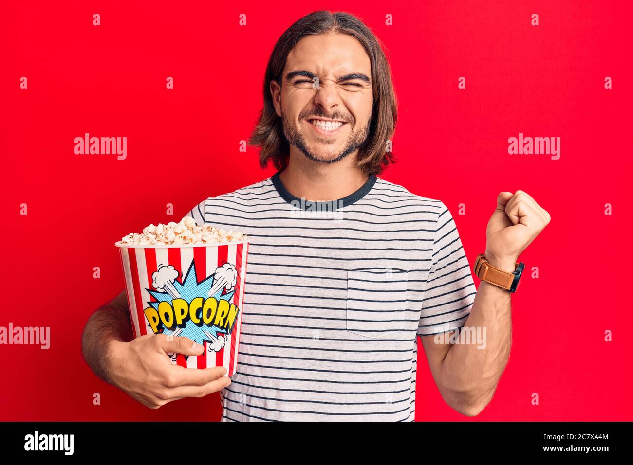 Young handsome man holding popcorn screaming proud, celebrating victory ...