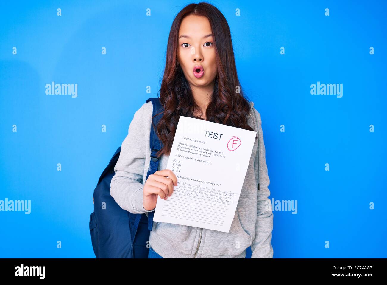 Young beautiful chinese girl showing a failed exam scared and amazed ...