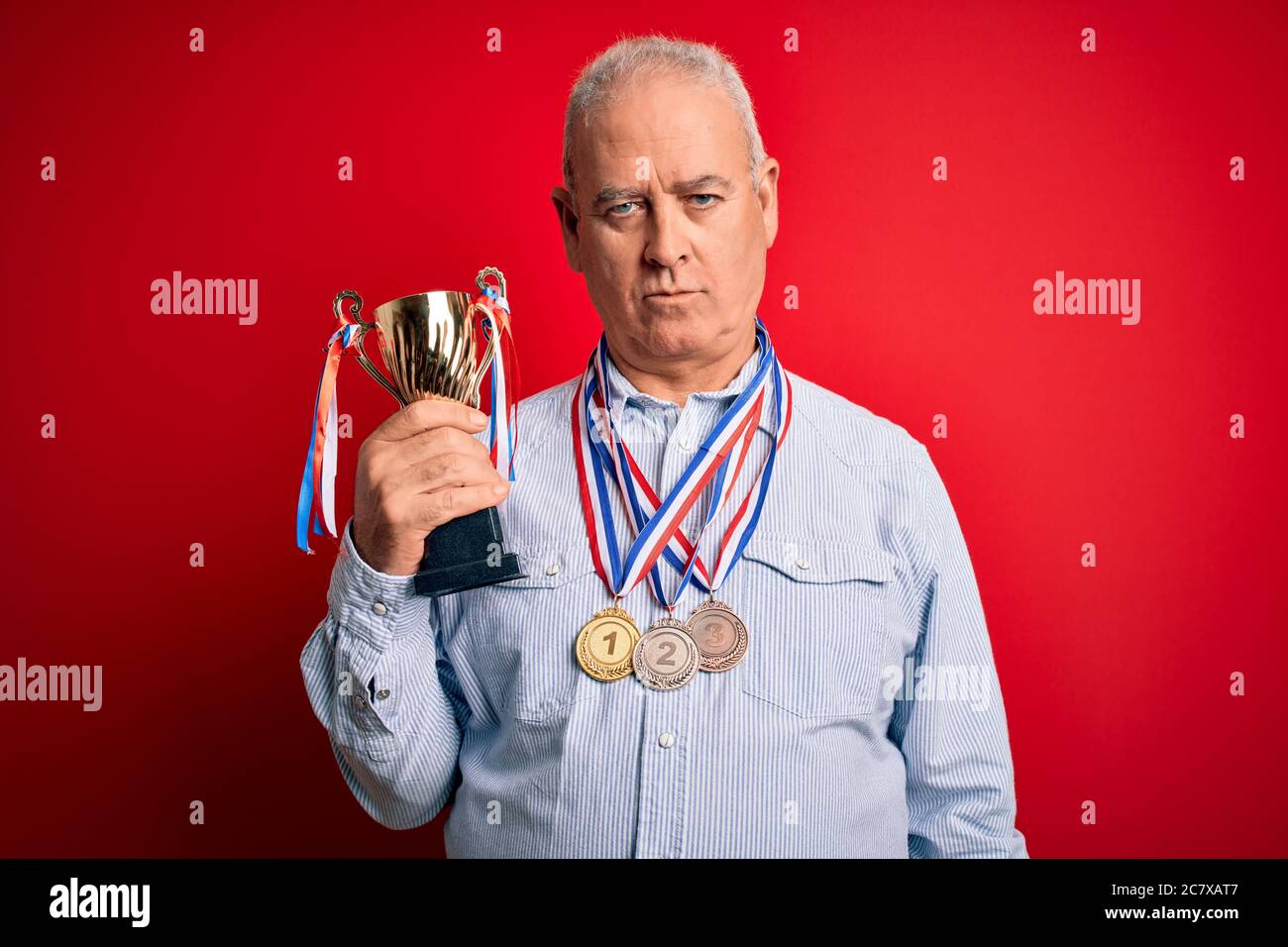 Middle age hoary successful man wearing medals holding trophy over ...