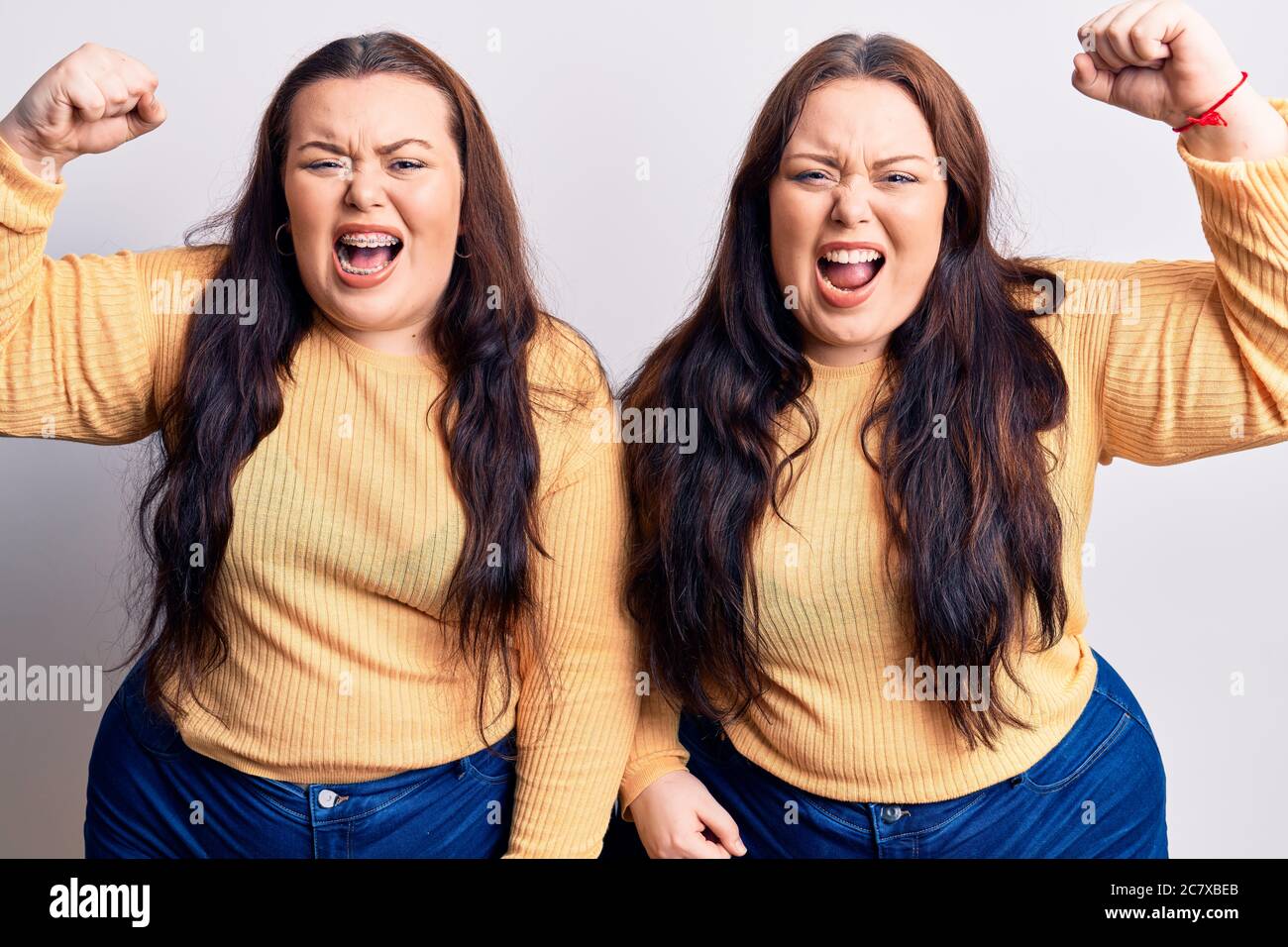 Young plus size twins wearing casual clothes angry and mad raising fist ...