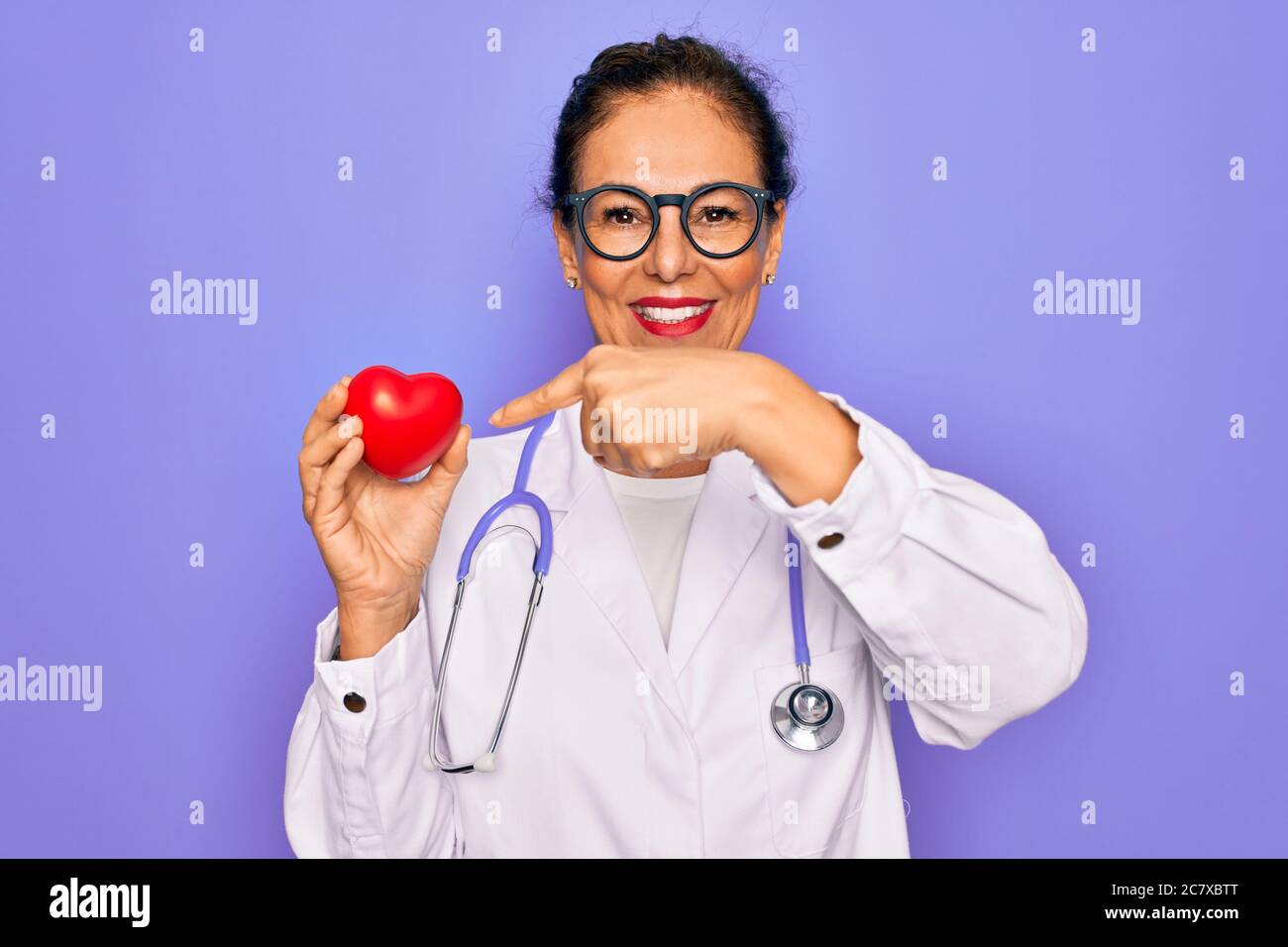 Middle age senior cardiologist doctor woman holding red heart over ...