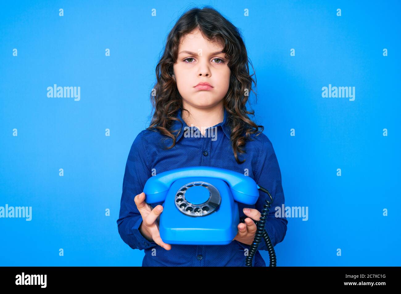 Cute hispanic boy with long hair holding vintage telephone depressed ...