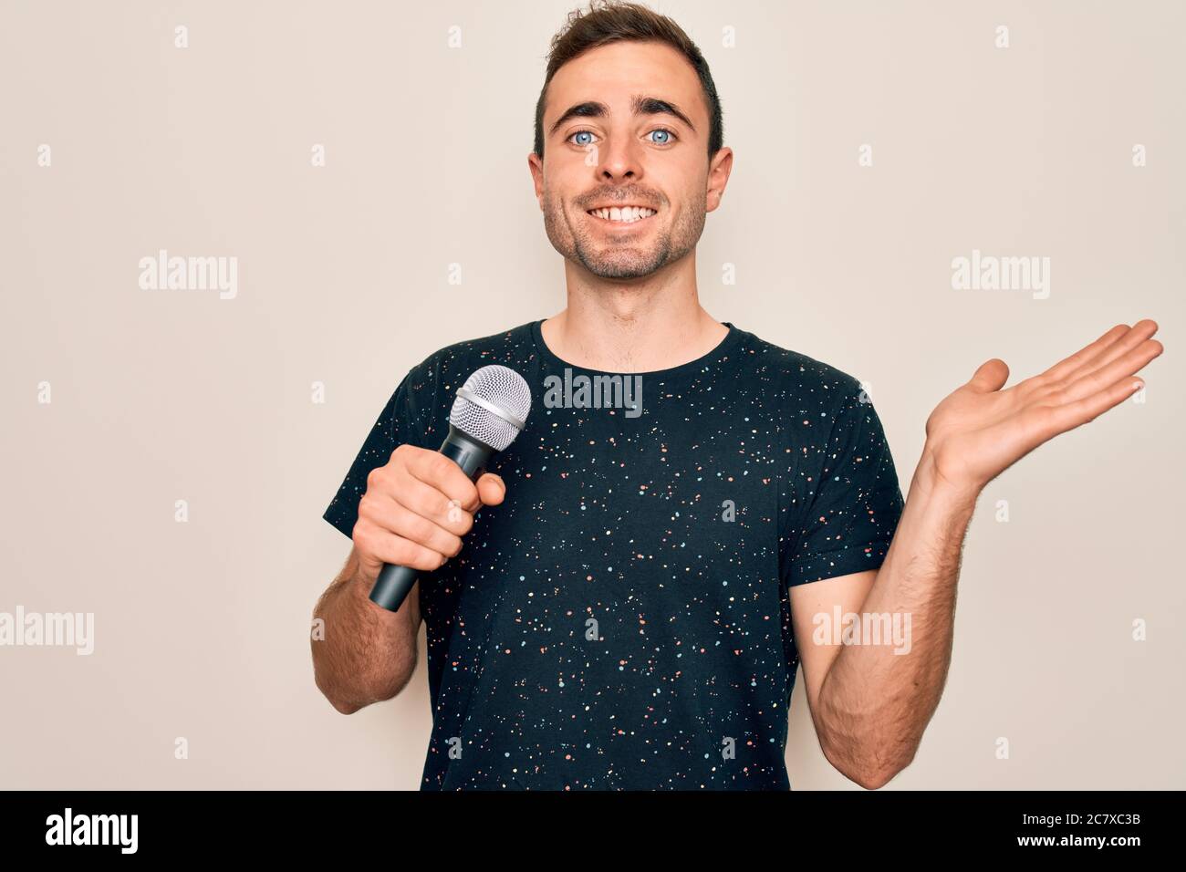 Young handsome singer man with blue eyes singing using microphone over white background very ...