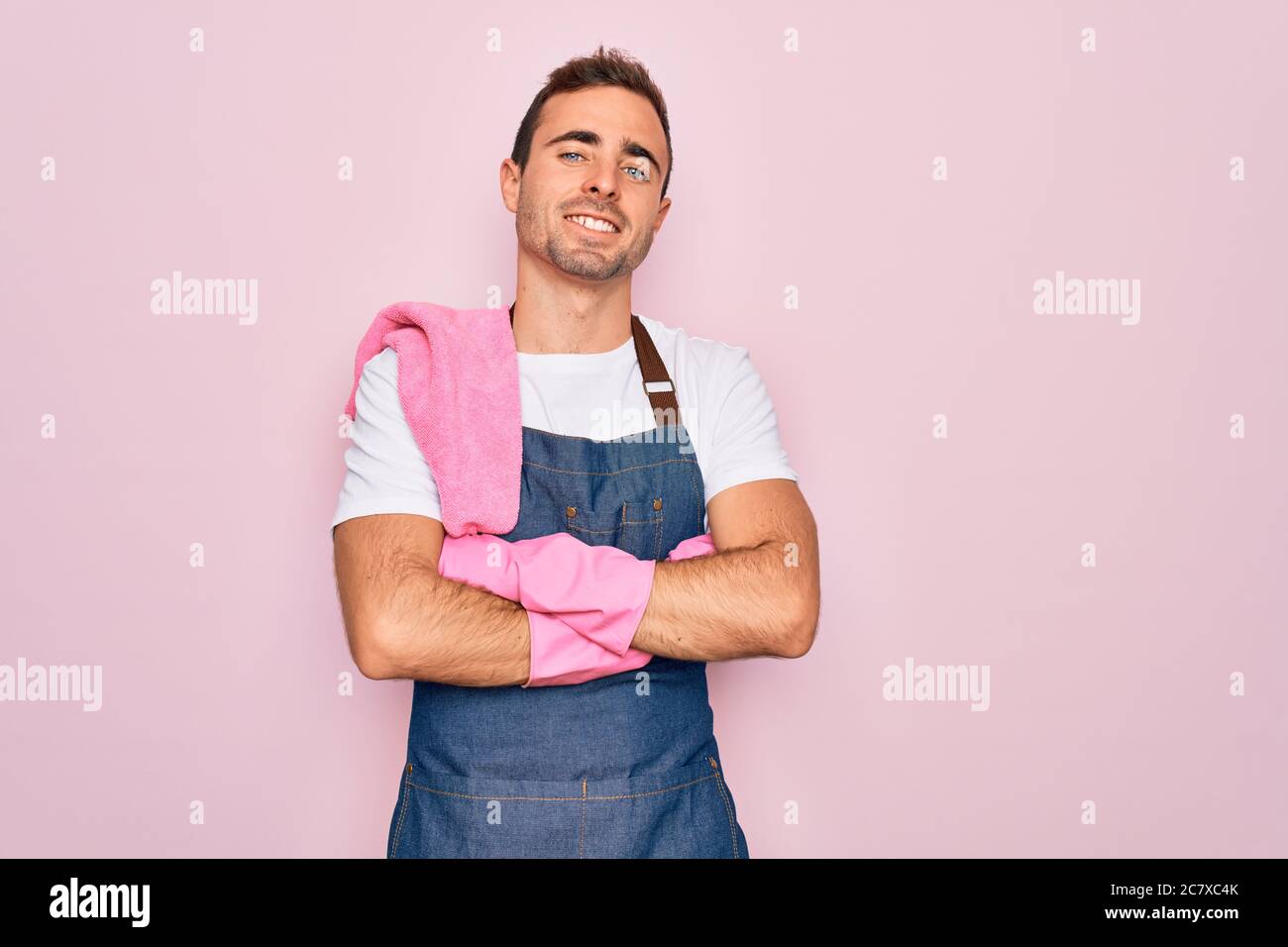Young cleaner man with blue eyes cleaning wearing apron and gloves over ...