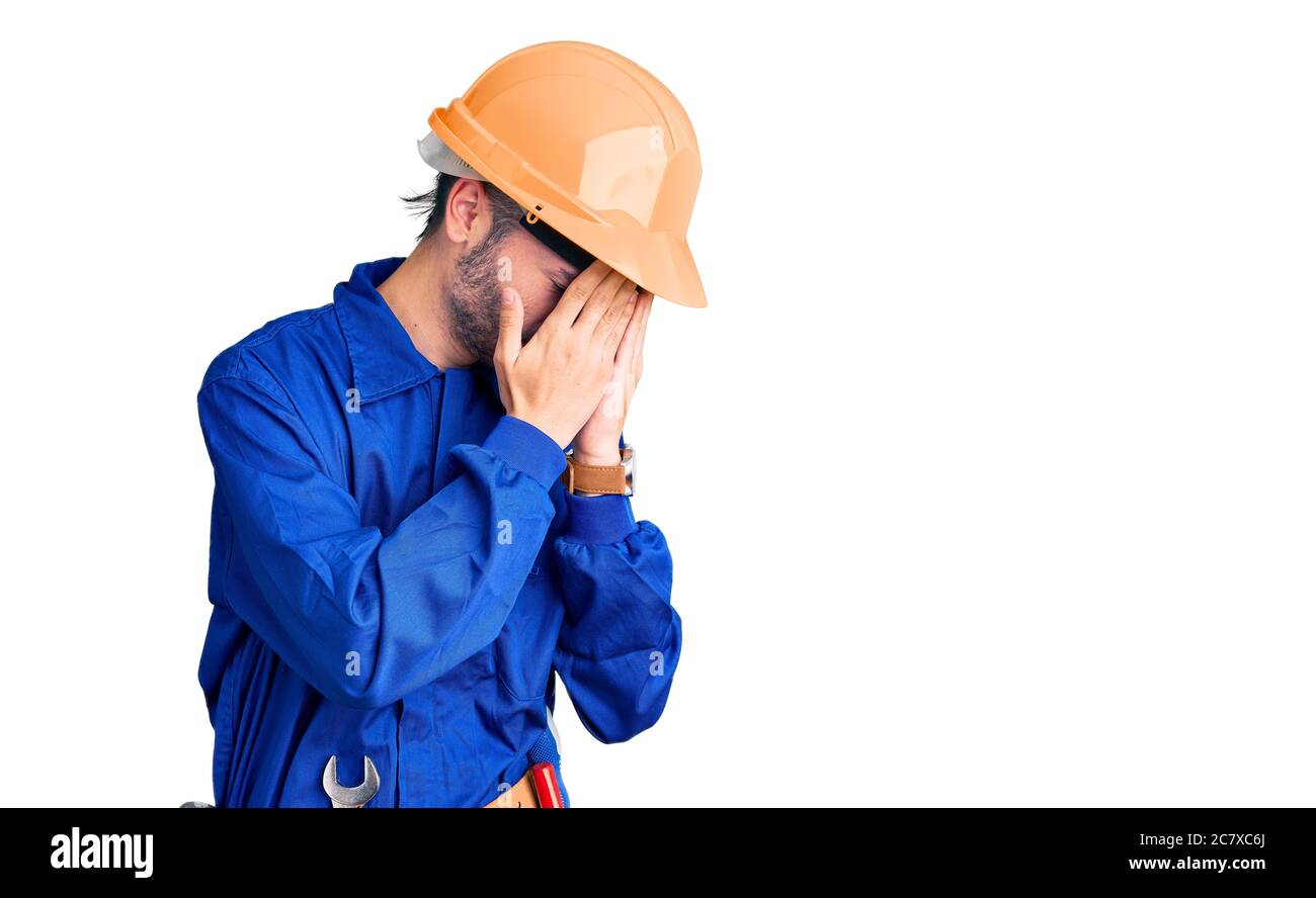 Young hispanic man wearing worker uniform with sad expression covering ...