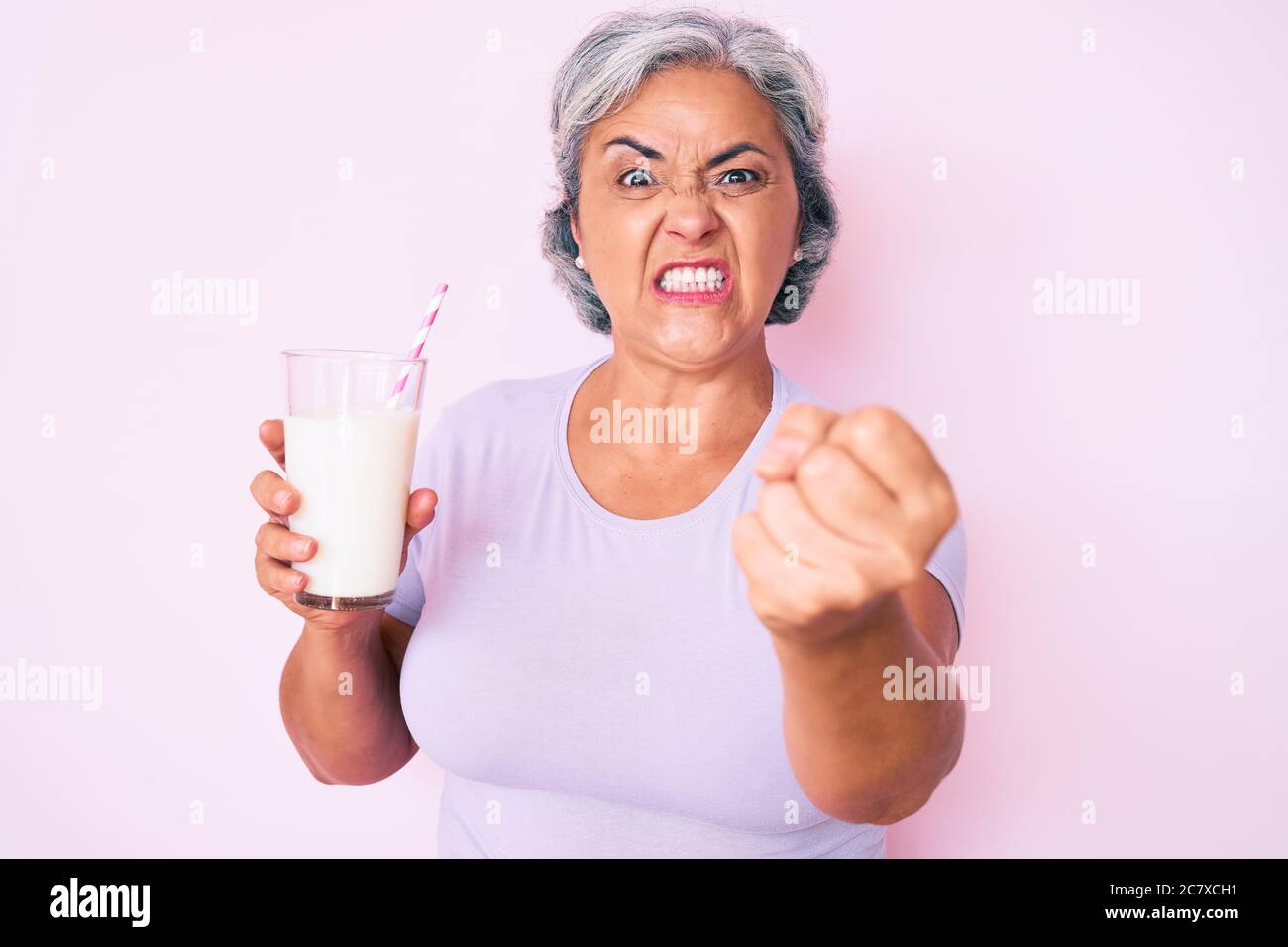 Senior hispanic woman holding glass of milk annoyed and frustrated ...