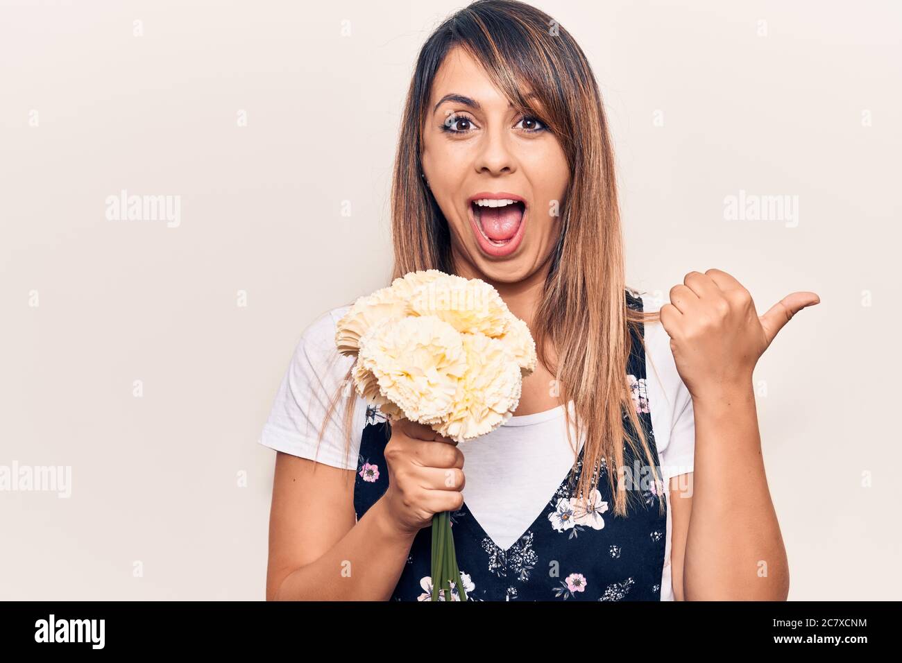 Young beautiful woman holding bouquet of flowers pointing thumb up to ...