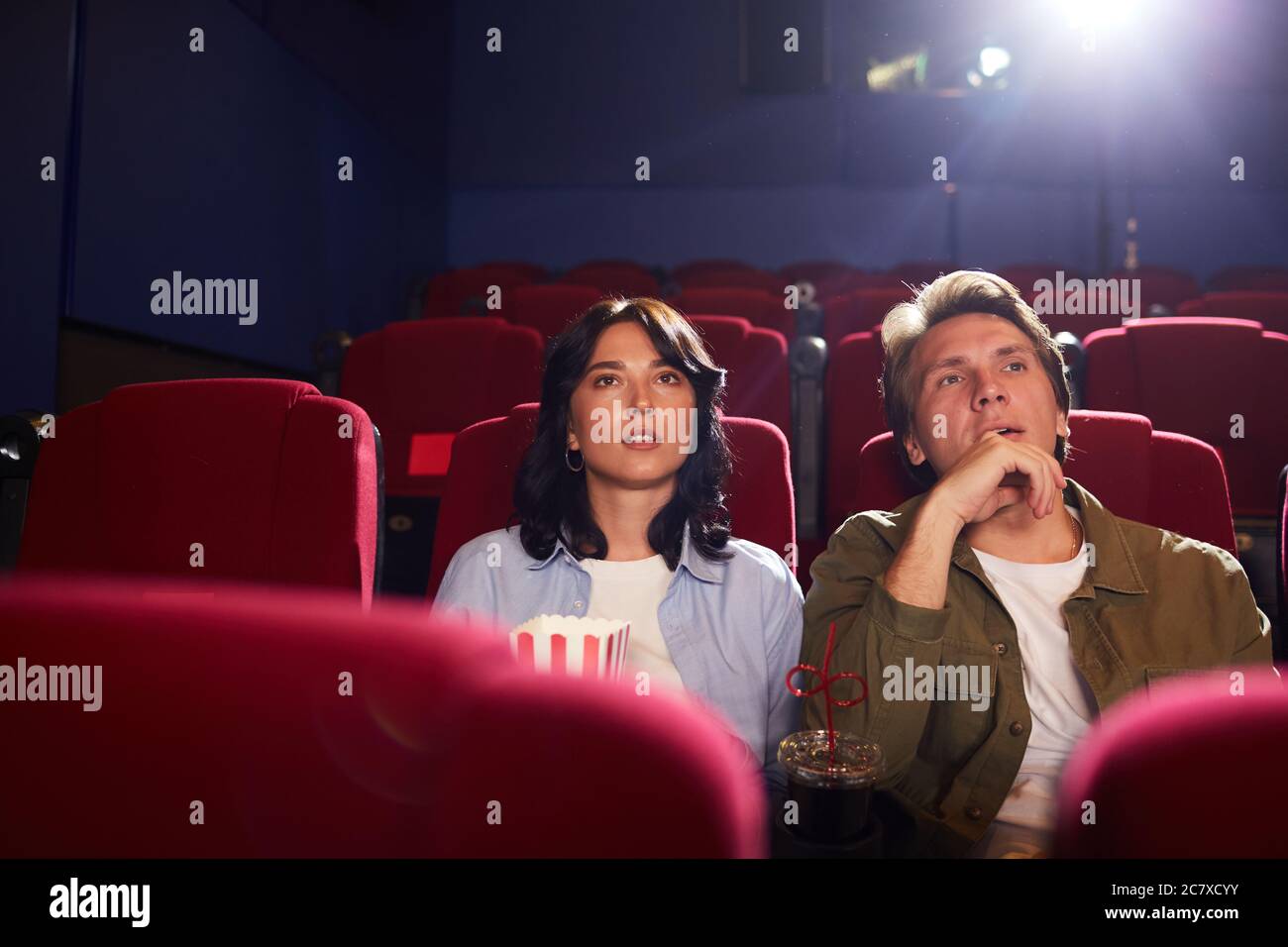 Portrait of young couple watching movie in cinema while enjoying ...