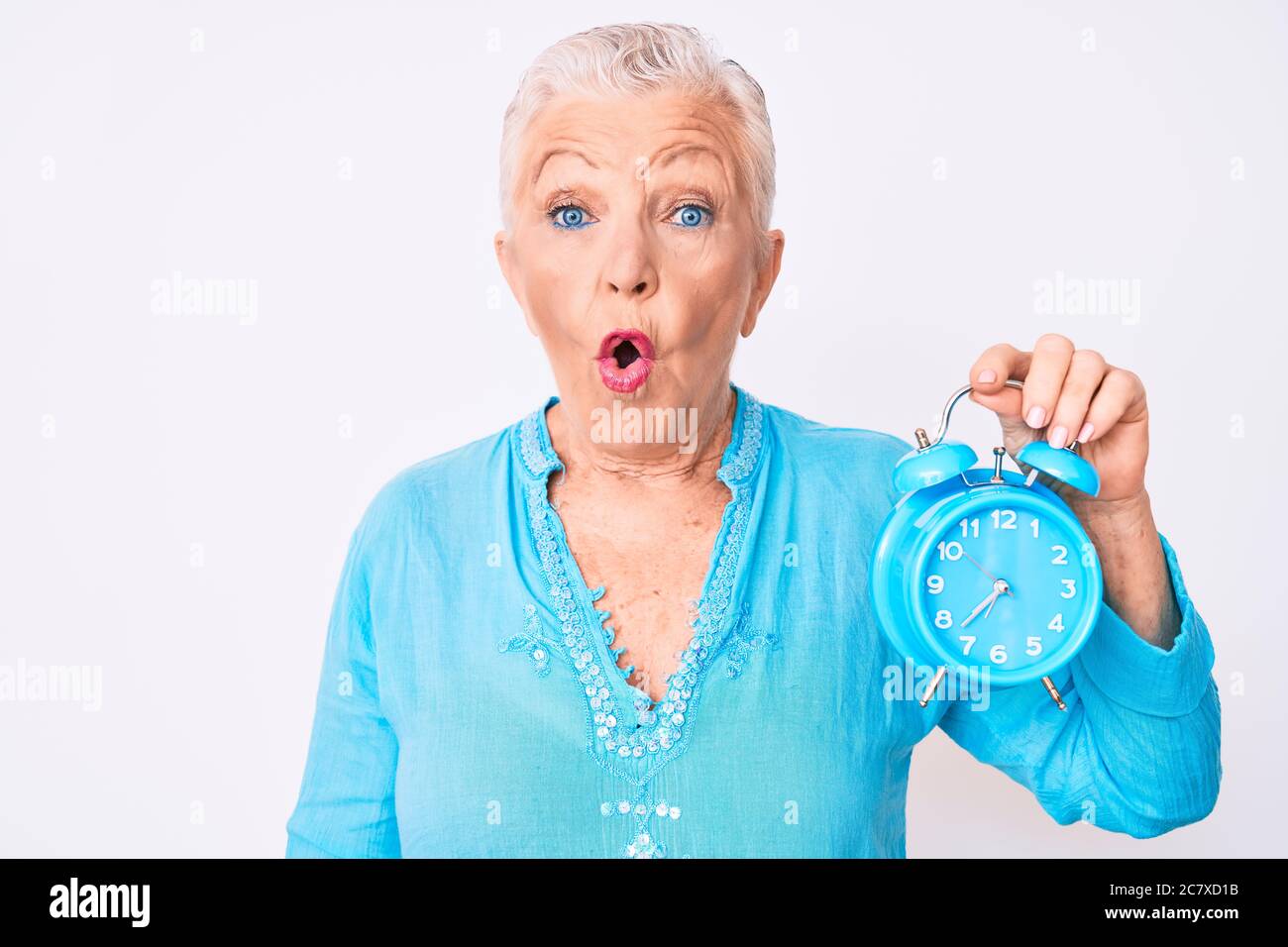 Senior beautiful woman with blue eyes and grey hair holding alarm clock ...