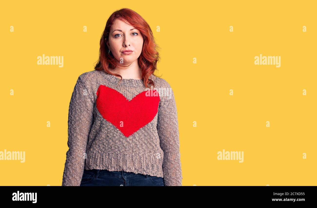 Young beautiful redhead woman wearing casual heart sweater with serious ...