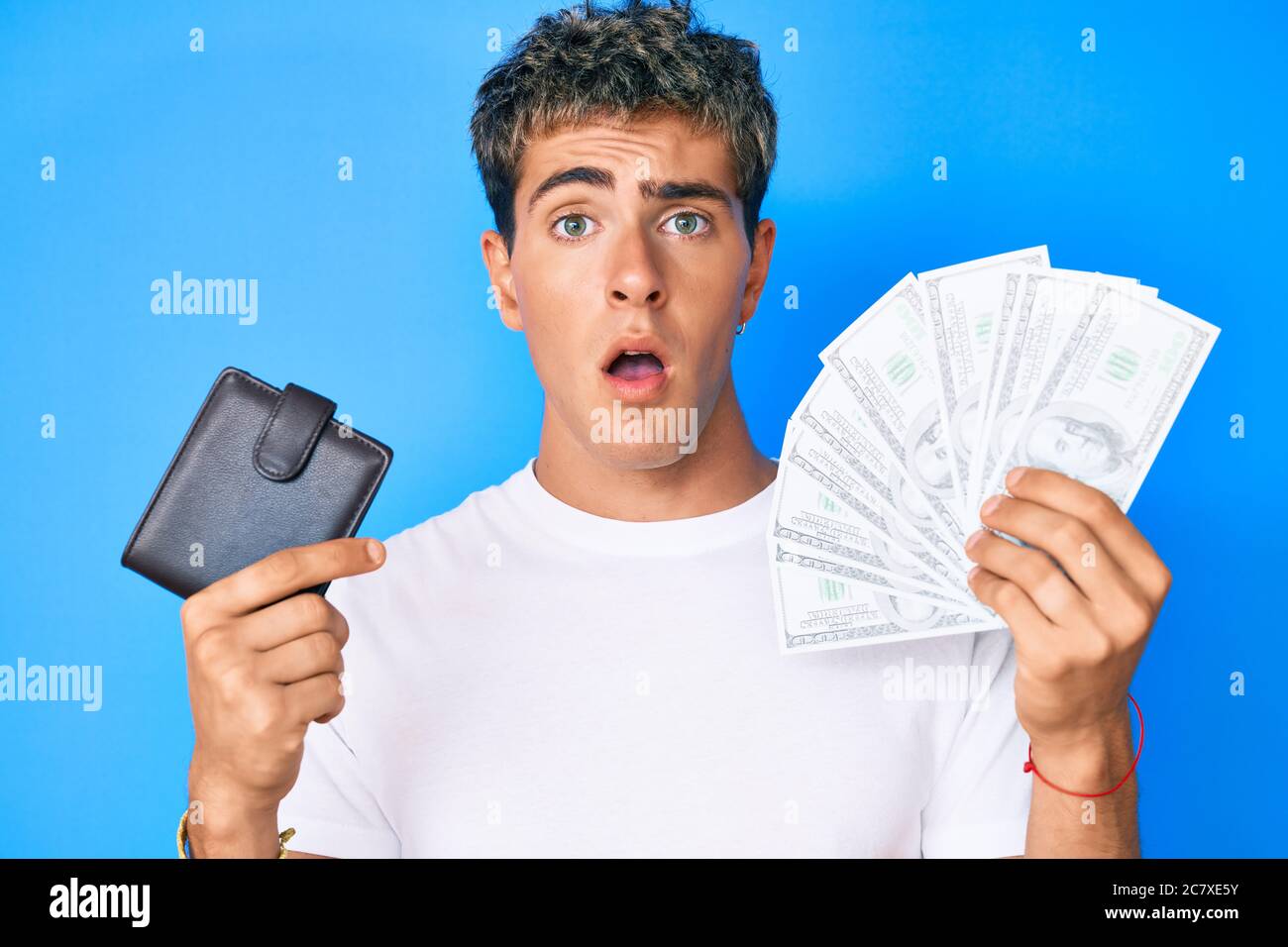 Young handsome man holding wallet and dollars banknotes afraid and ...