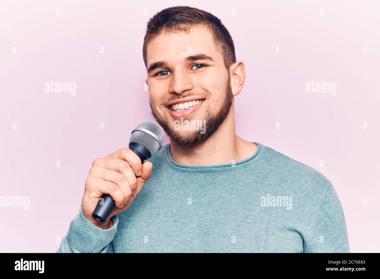Young handsome man singing song using microphone looking positive and ...