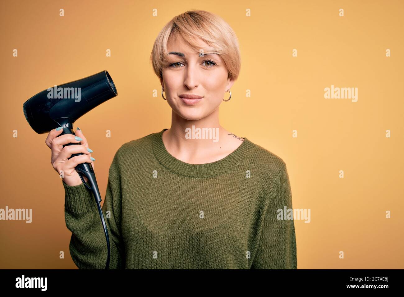 Young blonde woman with short hair drying her hair using hairdryer over ...