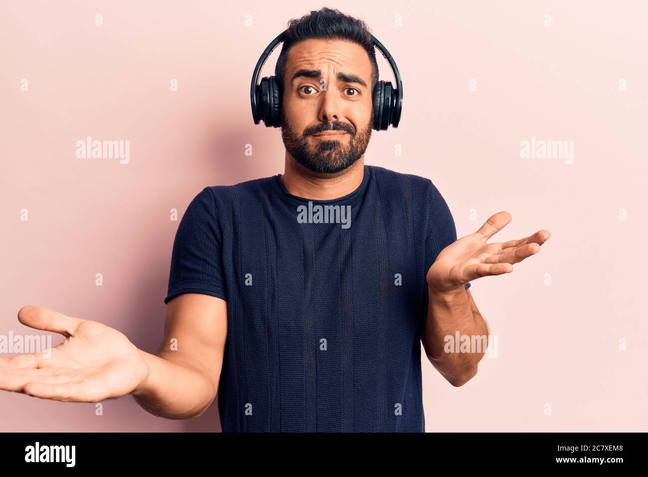 Young hispanic man listening to music using headphones clueless and ...